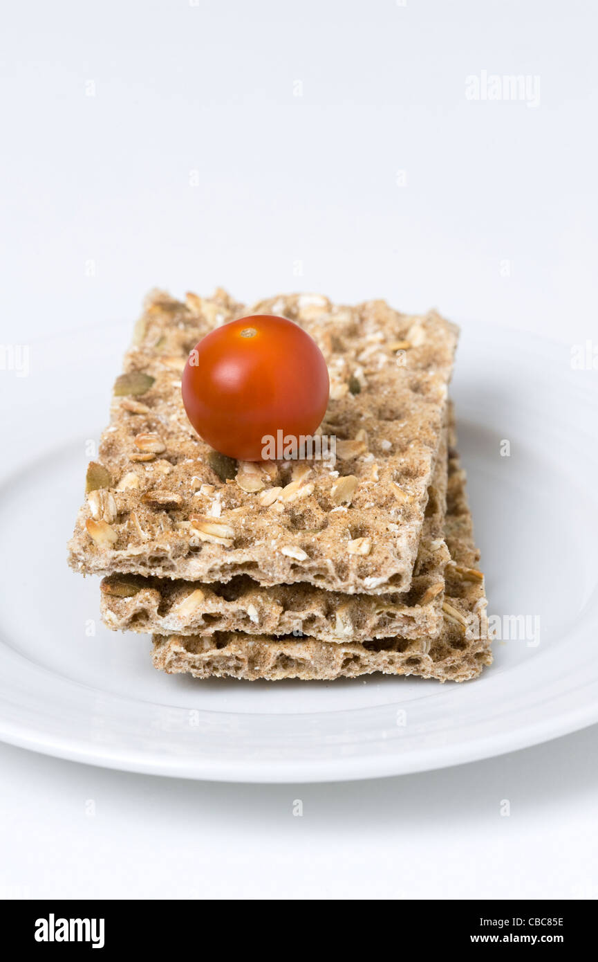 three ryveta rye based crackers with a single cherry tomato on a white ...