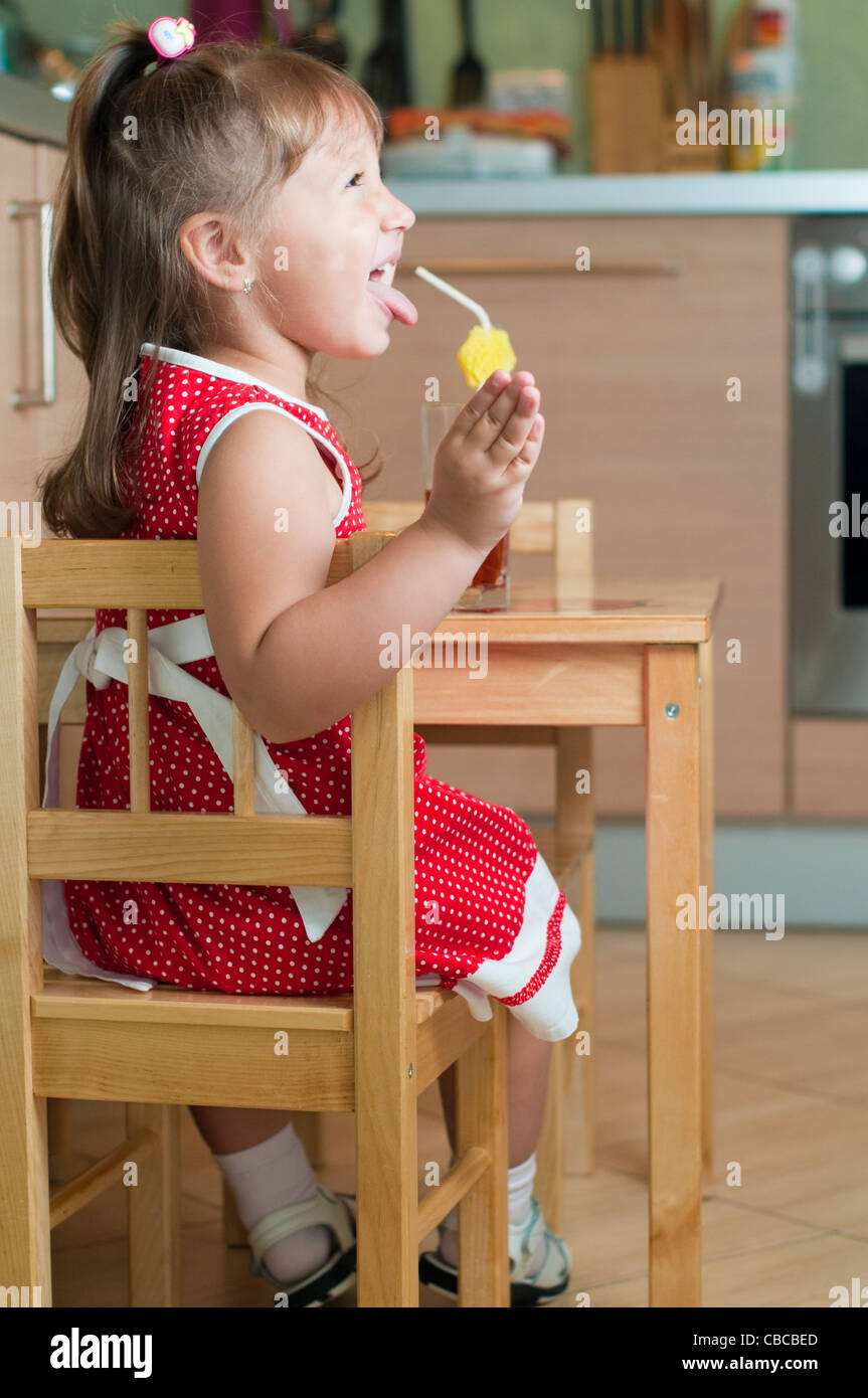 a happy little girl sitting at a table in a kitchen with a glass of ...