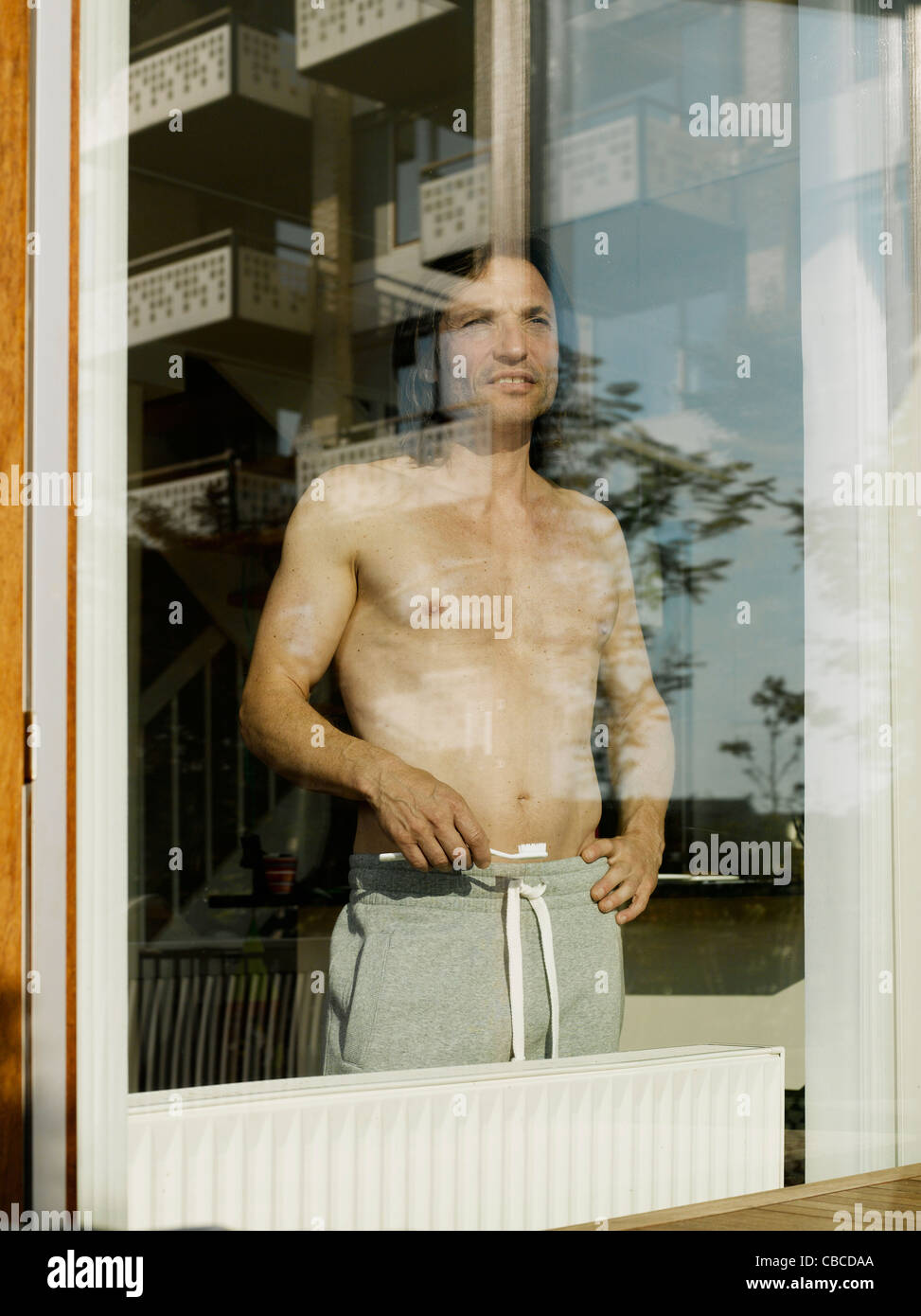Bare-chested man standing at window Stock Photo - Alamy