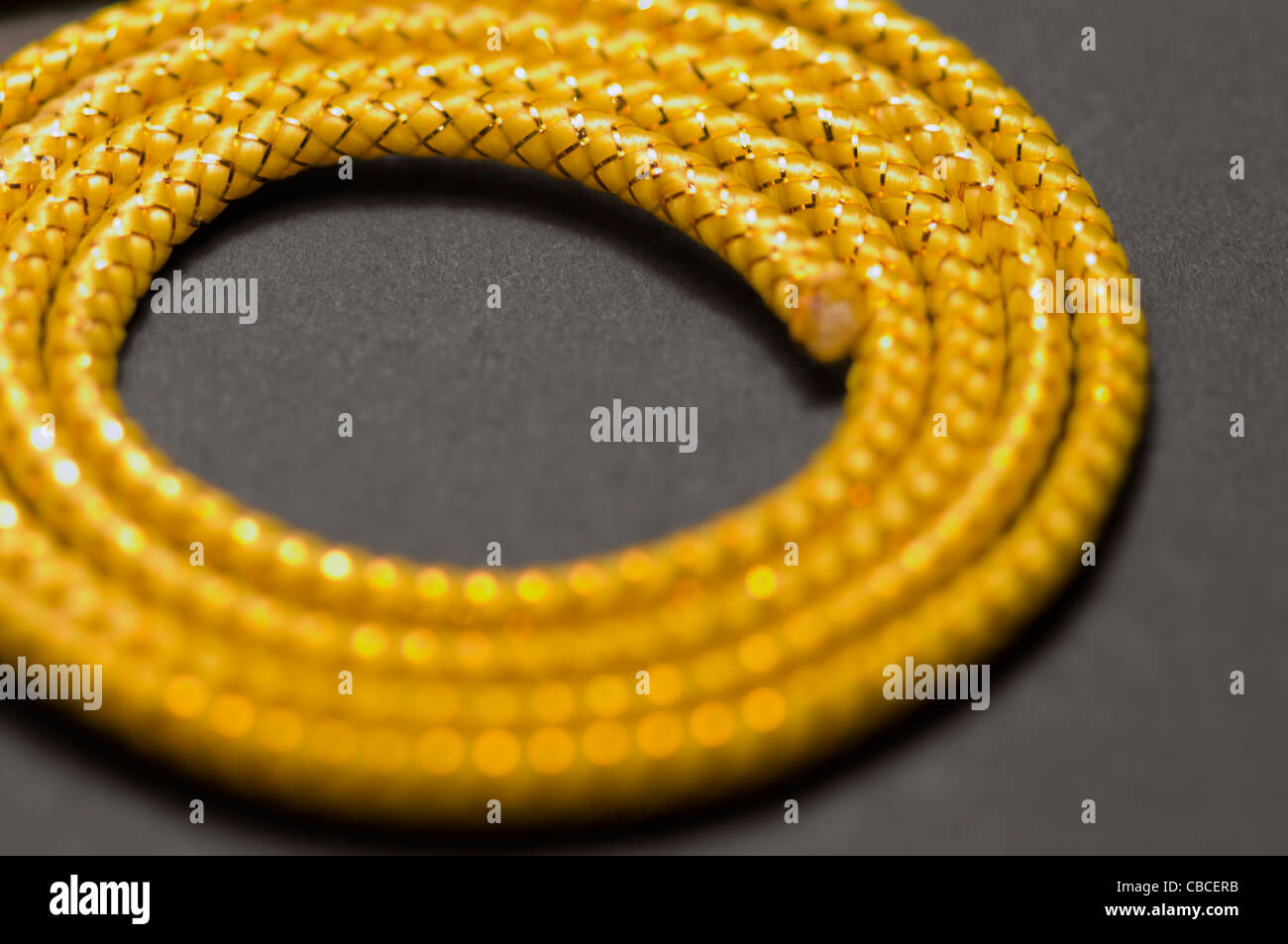 detail pf a rolled yellow cord with golden filament in dark grey back ...