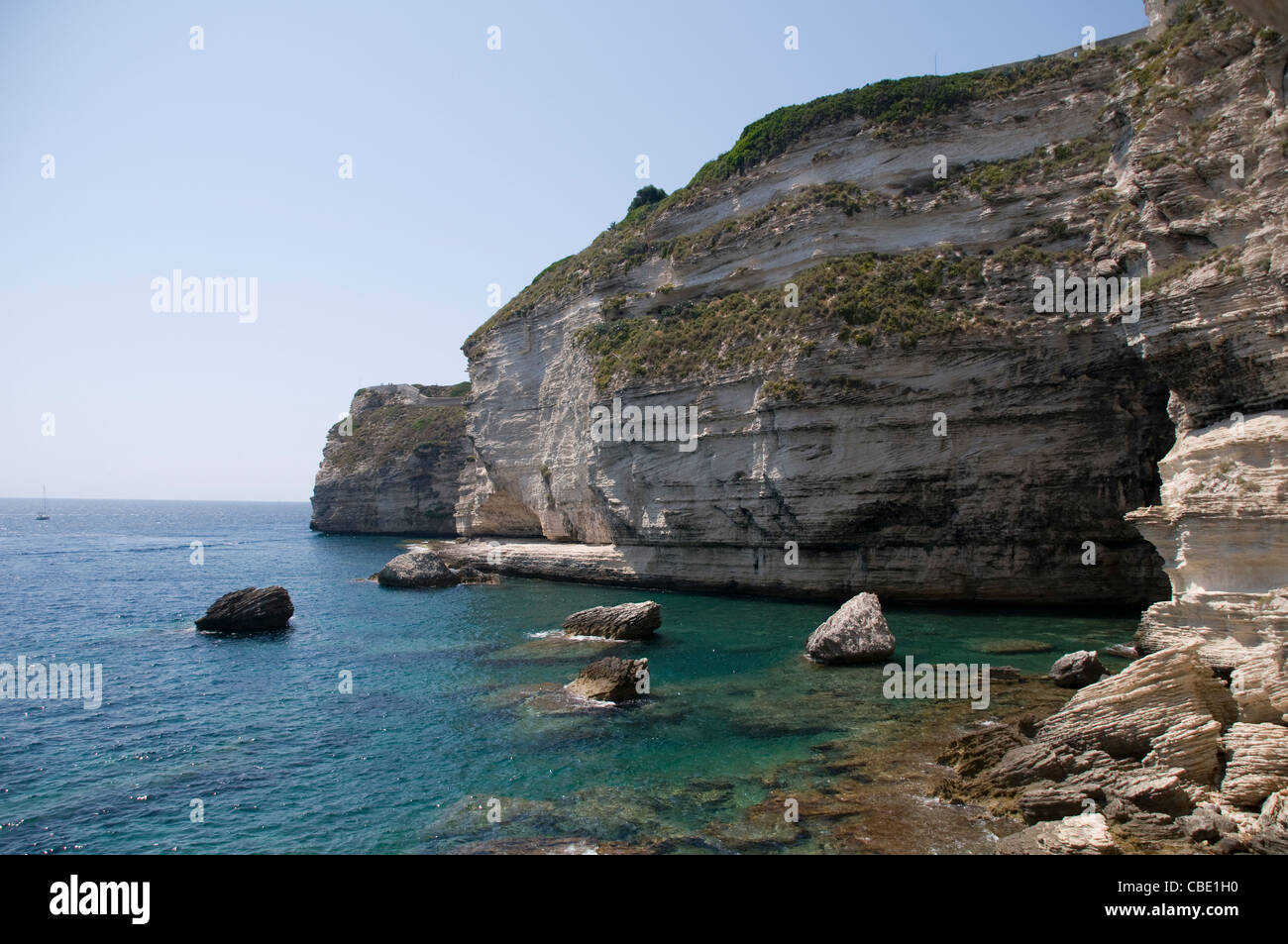 Coastal cave entrance in cliff face with crystal blue water and rocks ...