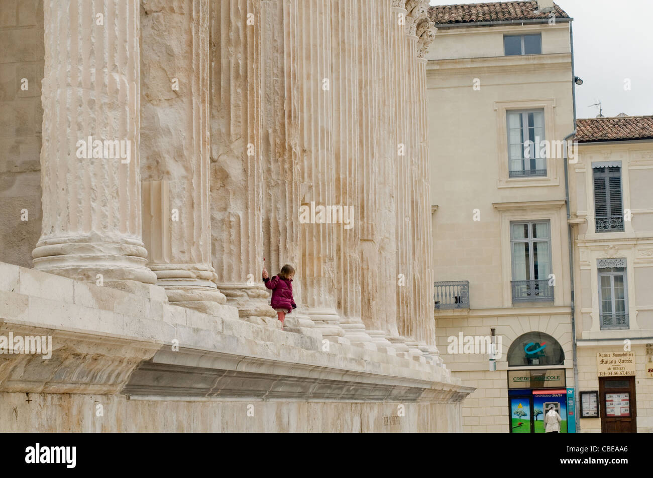Very young girl standing between columns, peers over the side of the ...
