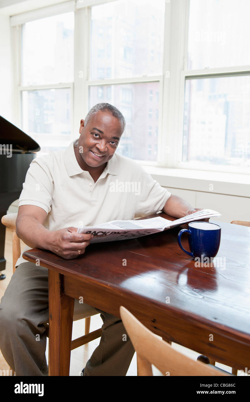A mature man sitting at dining table holding a newspaper Stock Photo ...