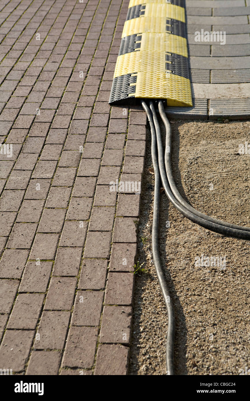 Cables coming from a speed bump on a cobblestone road Stock Photo - Alamy
