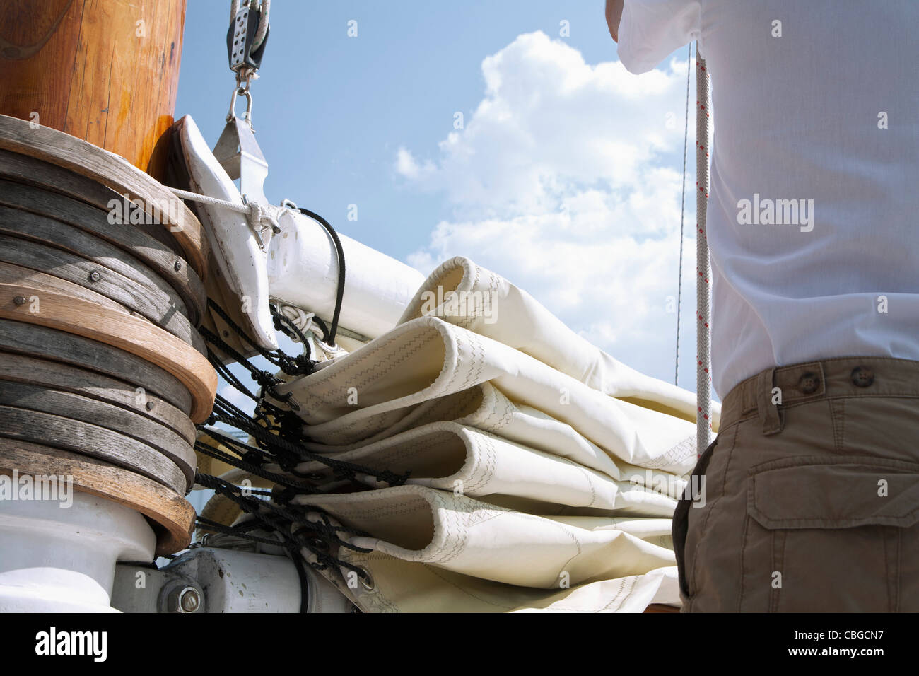 Rear midsection of man next to sail and mast of a passenger sailboat ...
