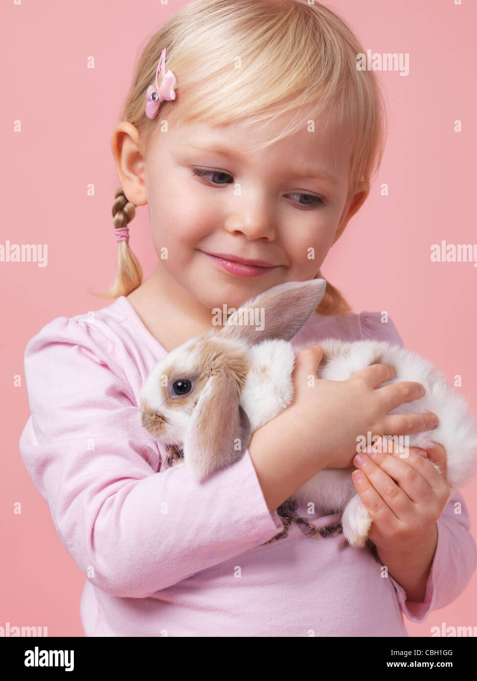 Portrait of a three year old girl holding a pet rabbit isolated on pink ...