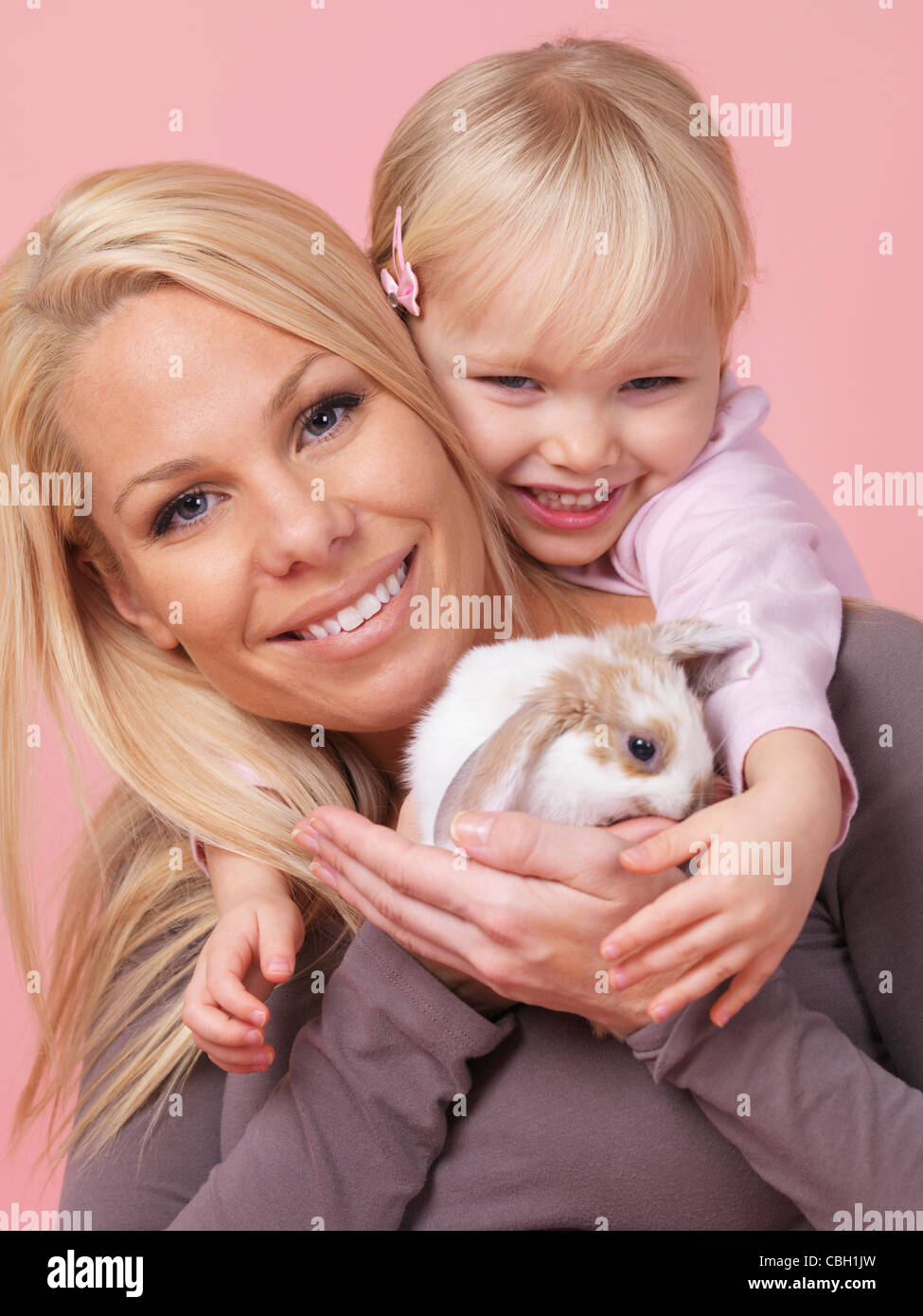 Portrait of a smiling three year old girl with her mother holding a pet ...