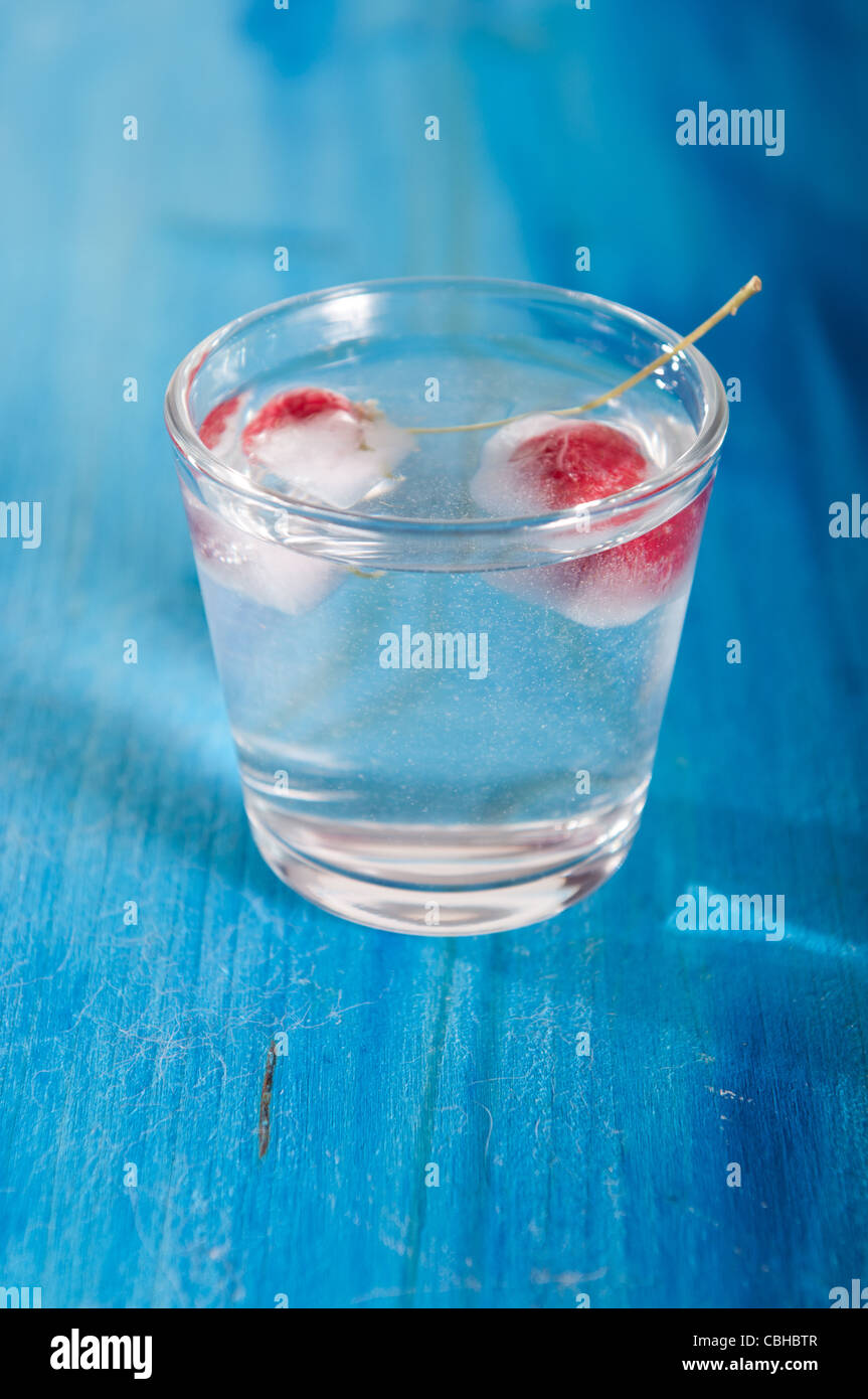 Raspberries in ice cubes put in water on blue background. Refreshment ...