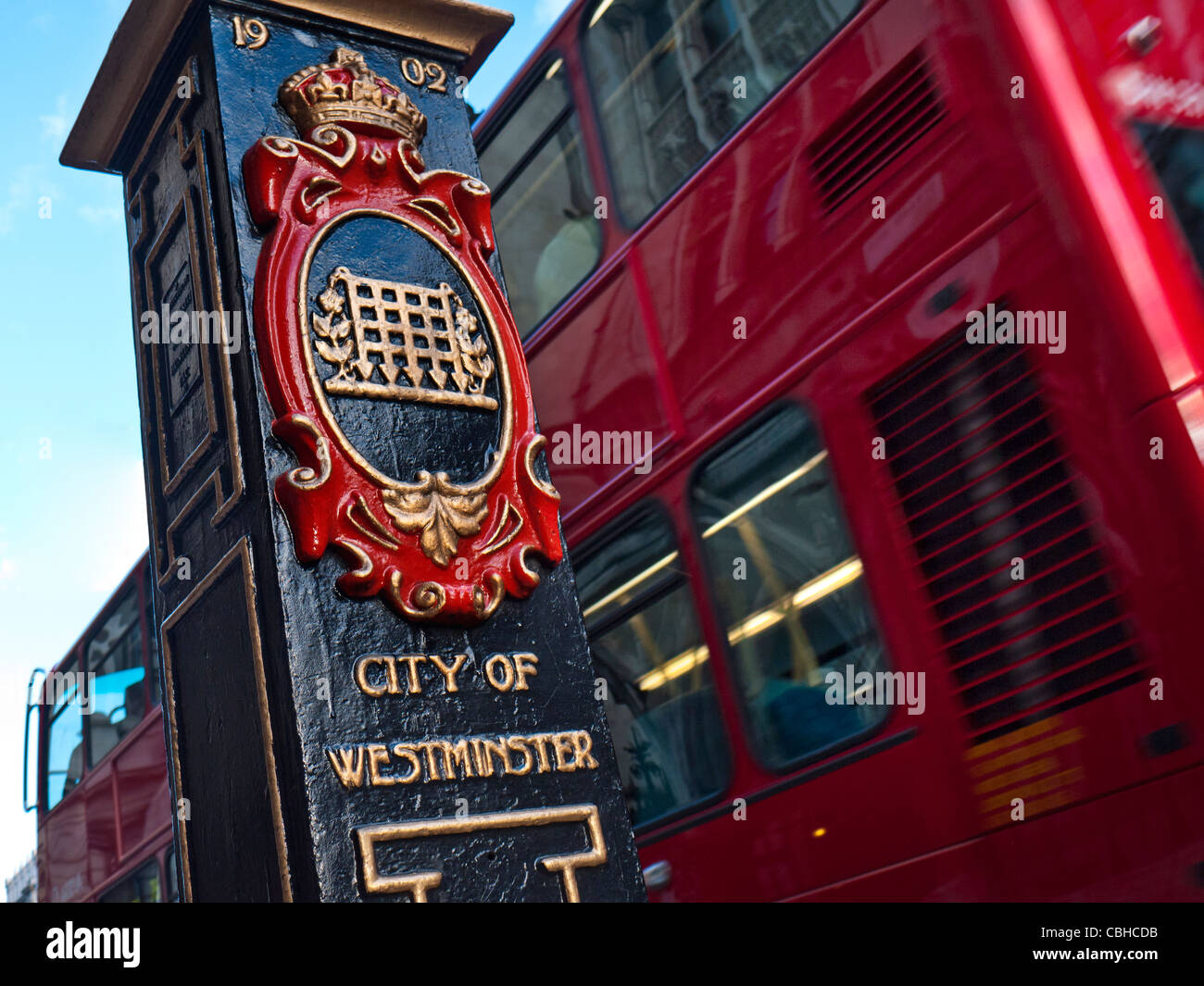 Ornate historic post marker with 1902 heraldic coat of arms and red bus ...