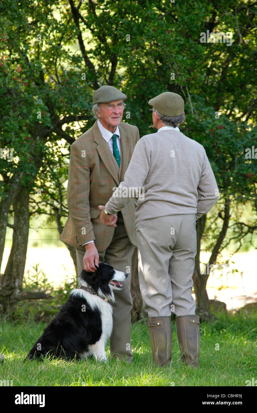 Two Shepherds talking and sheep dog in front of trees at Calbeck Sheep ...