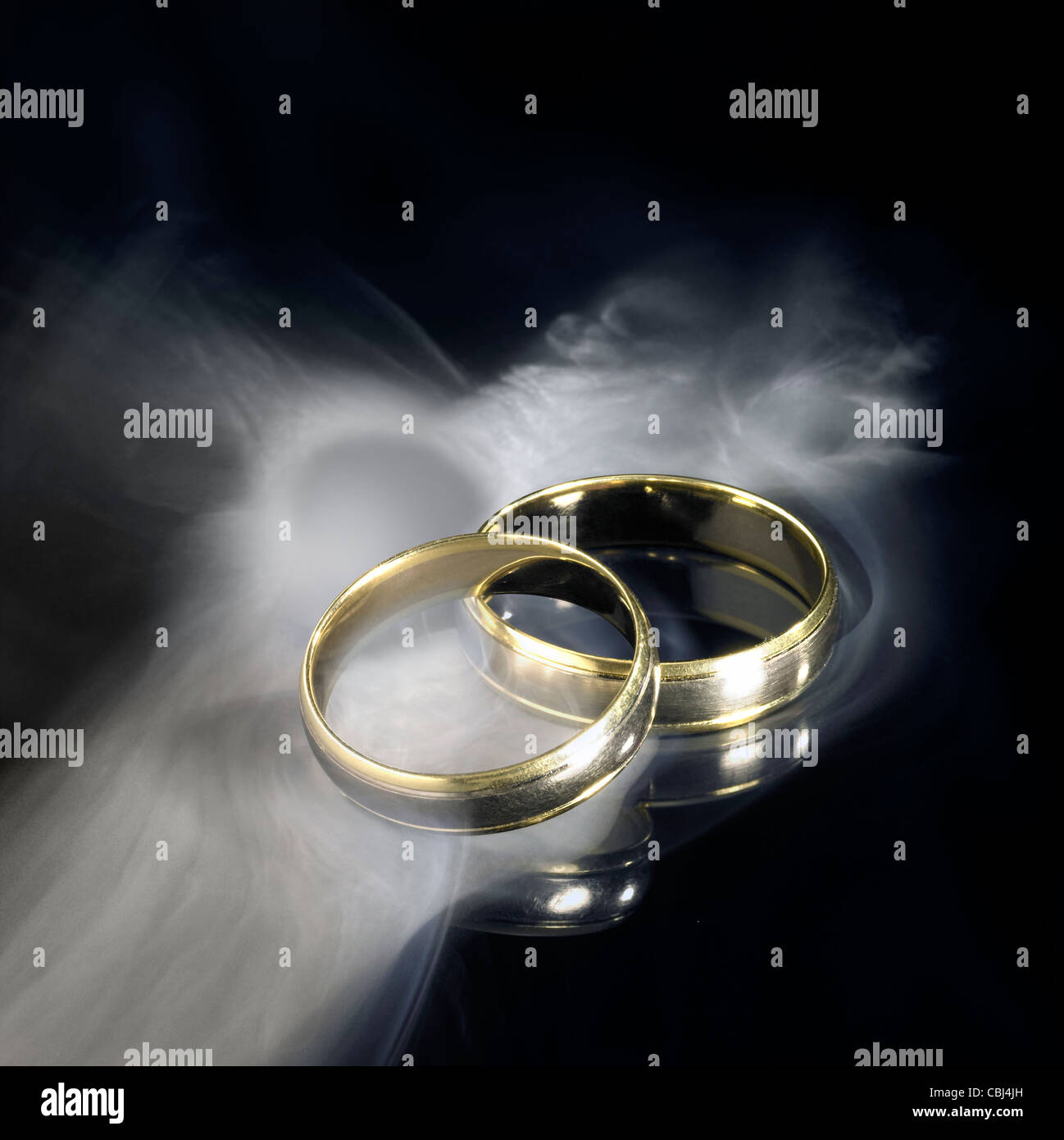studio photography of two golden wedding rings and smoke in black ...