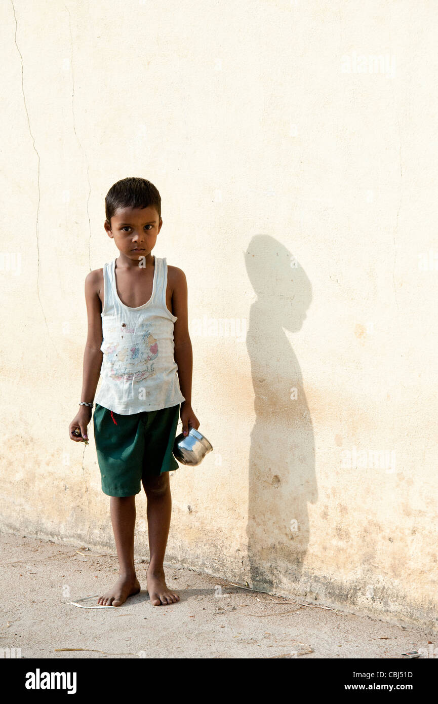 Young poor rural Indian village boy standing next to a wall holding a ...