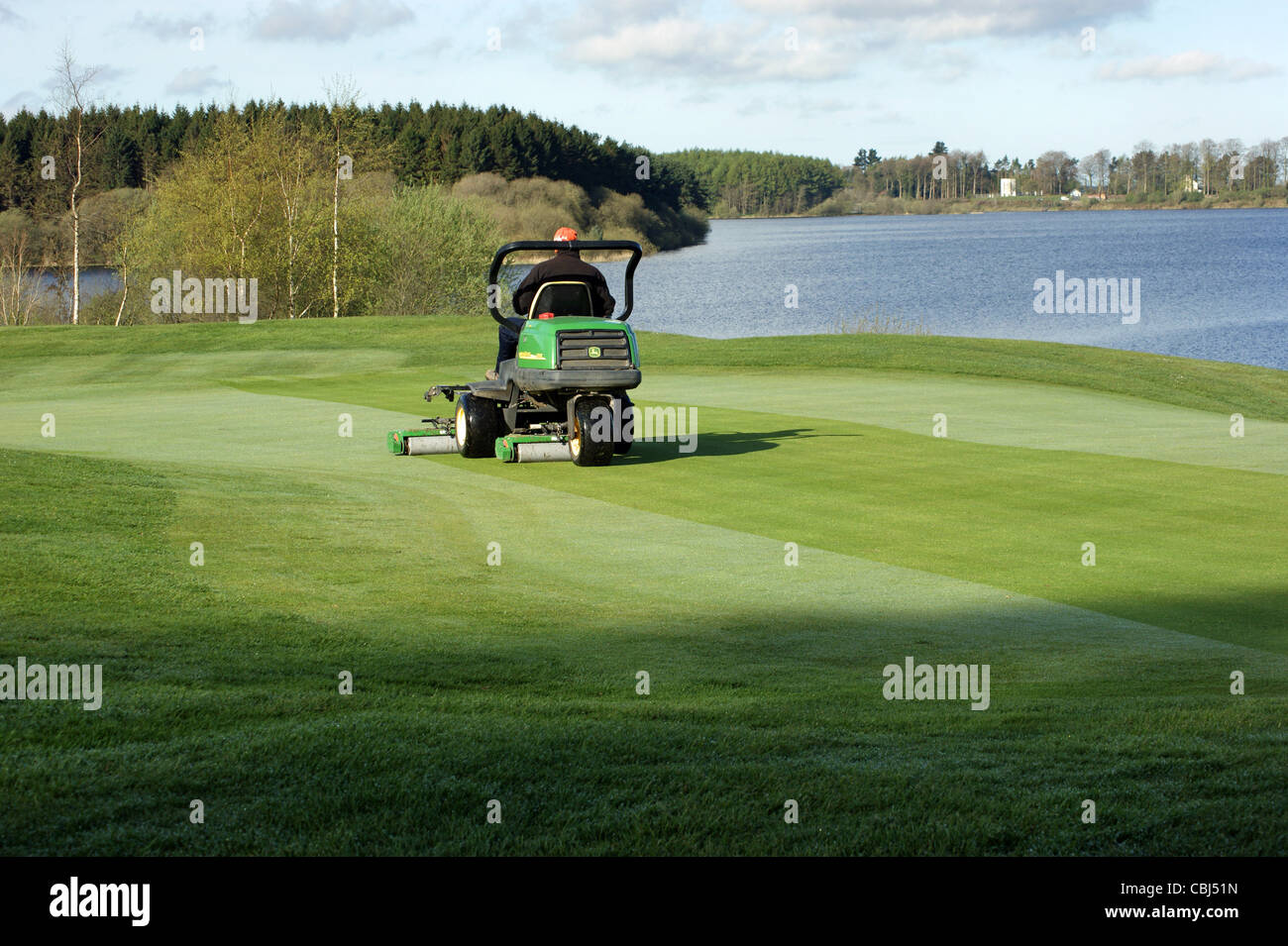 A golf course worker mows the grass of a green, in the early morning ...