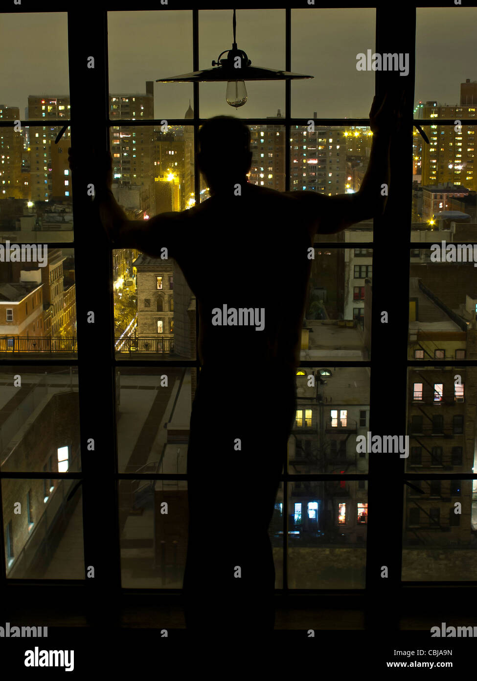 Silhouette of Man at window at night overlooking Nw York City, New York ...