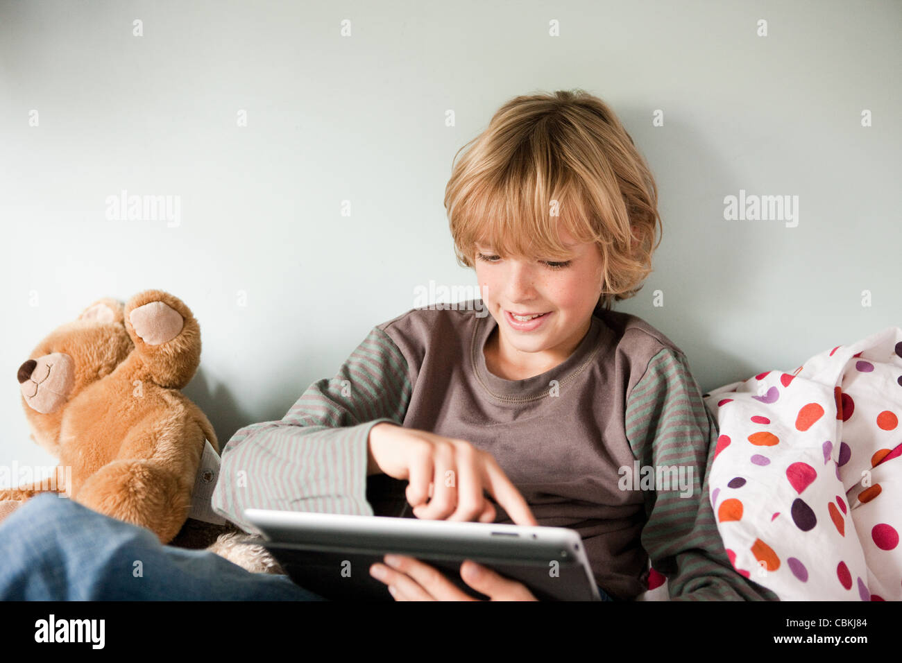 Young boy using a digital tablet while sitting on his bed Stock Photo ...