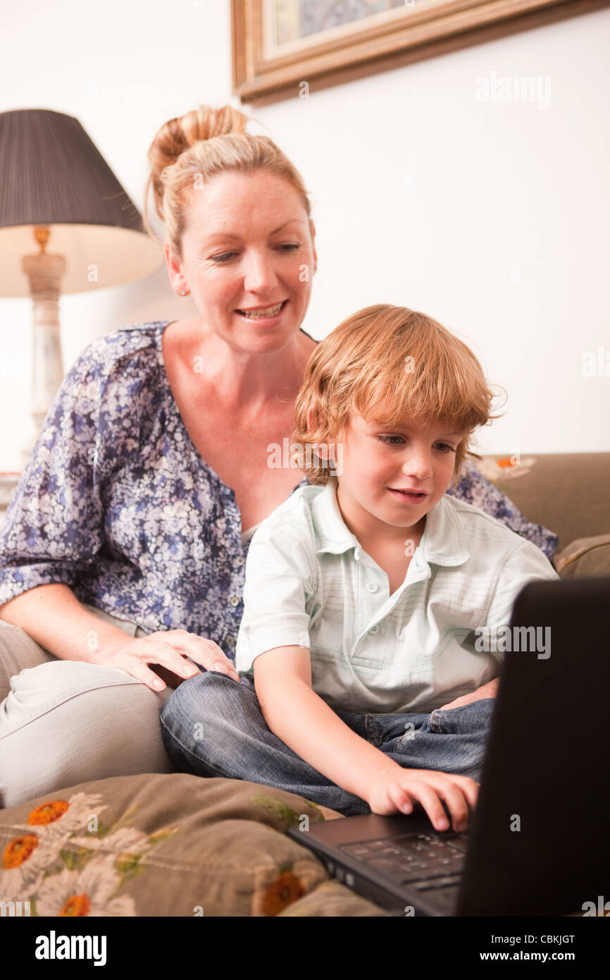 Young boy using laptop with mother looking on encouragingly Stock Photo ...