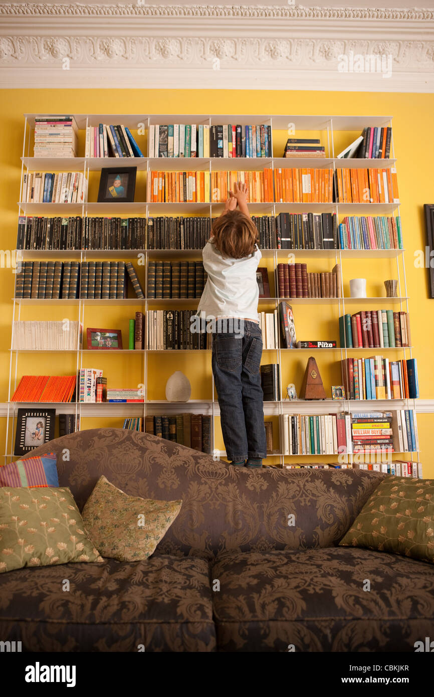 Young boy reaching up to get a book from a bookcase Stock Photo - Alamy