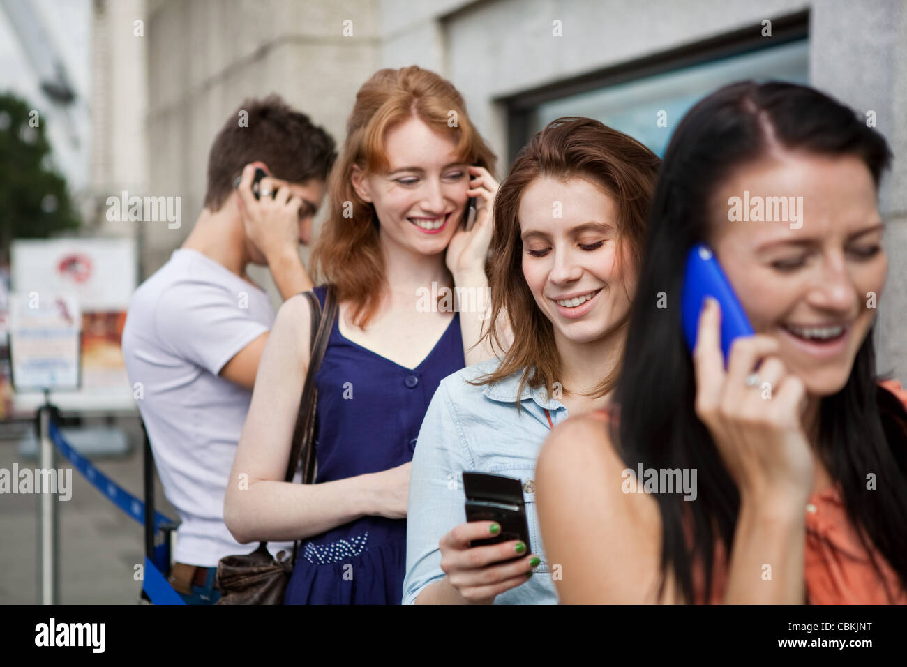 Four people in a queue, all using mobile phones Stock Photo - Alamy