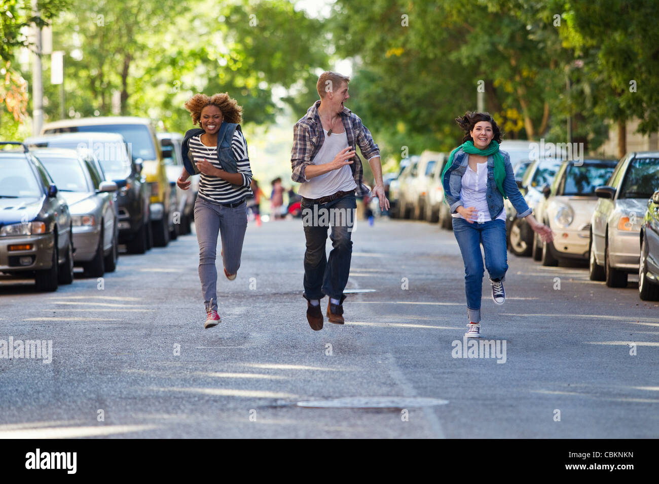 Three friends running through city street Stock Photo - Alamy