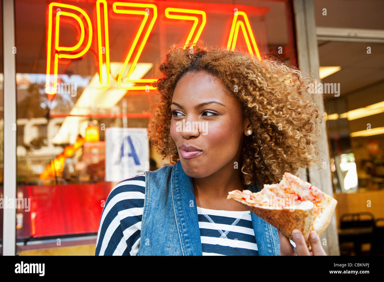Young woman eating pizza slice Stock Photo - Alamy