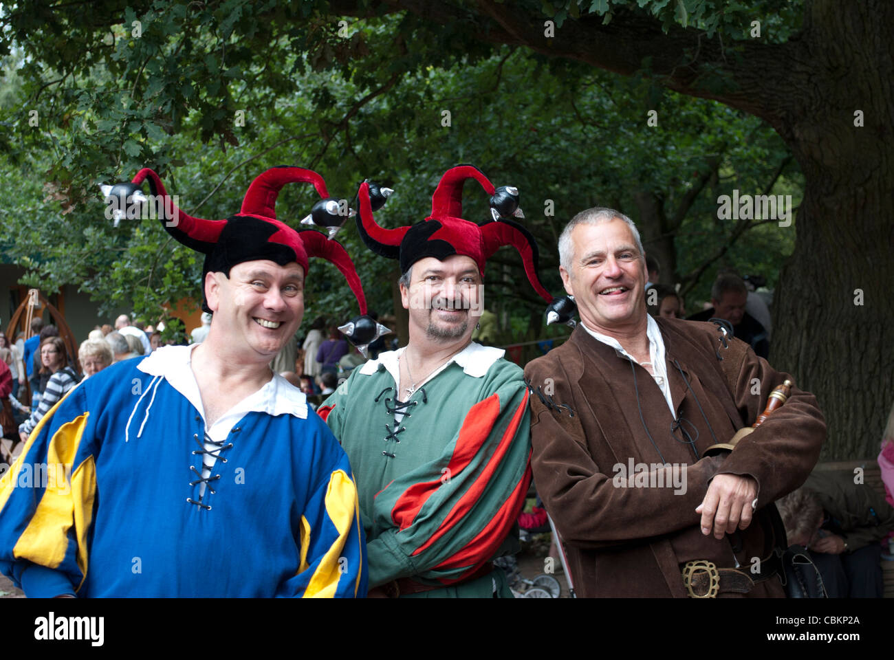 Three men in medieval clothing, two with jester hats on, smiling and ...