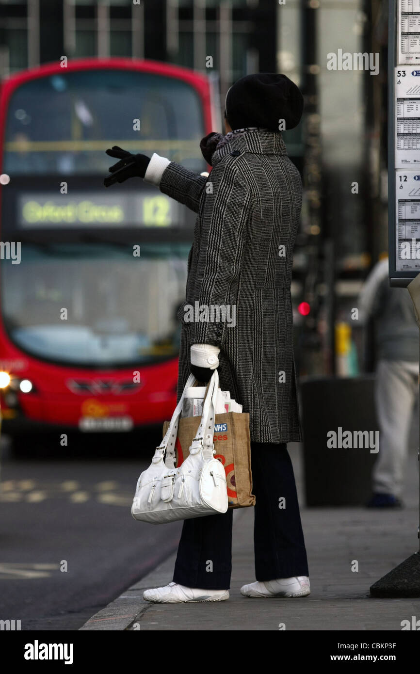 a person waiting at a bus stop and hailing a red London bus Stock Photo ...