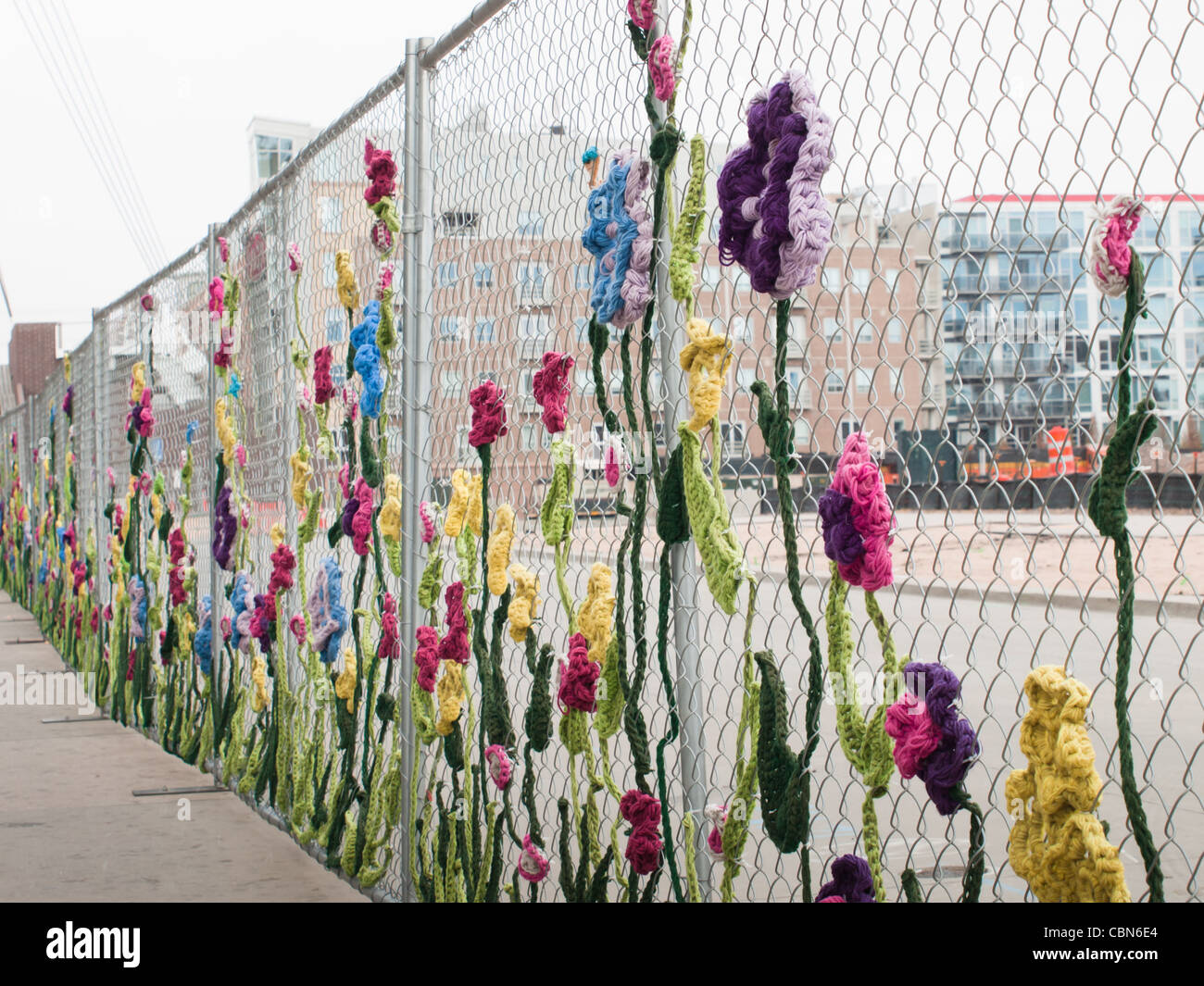 Construction fence covered with crocheted garden creatures like bugs ...