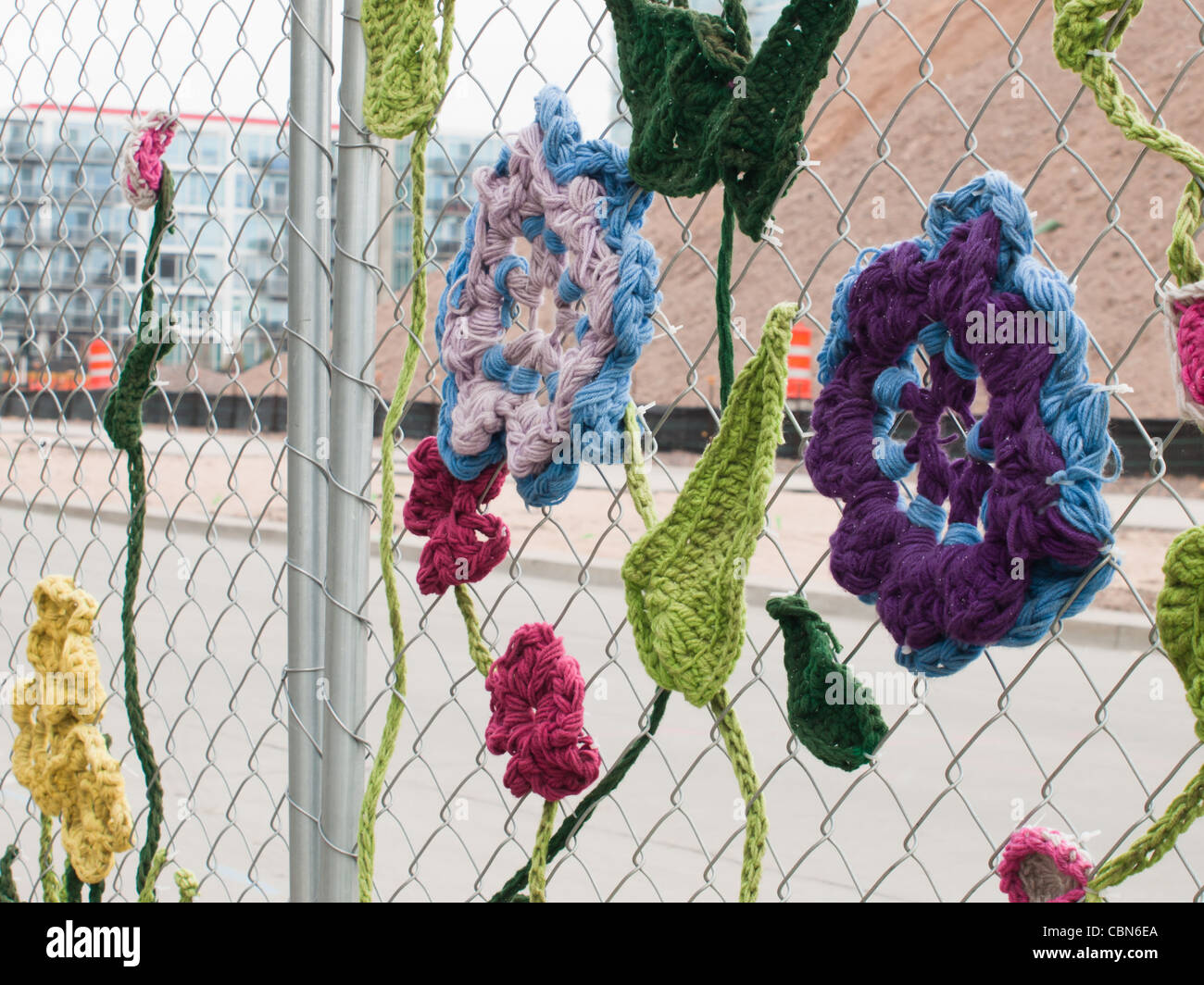 Construction fence covered with crocheted garden creatures like bugs ...