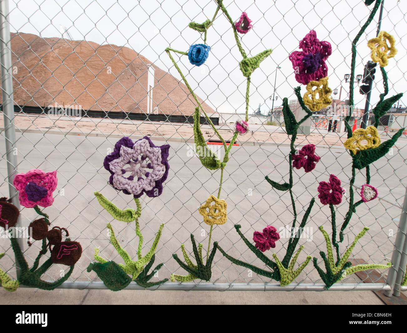 Construction fence covered with crocheted garden creatures like bugs ...