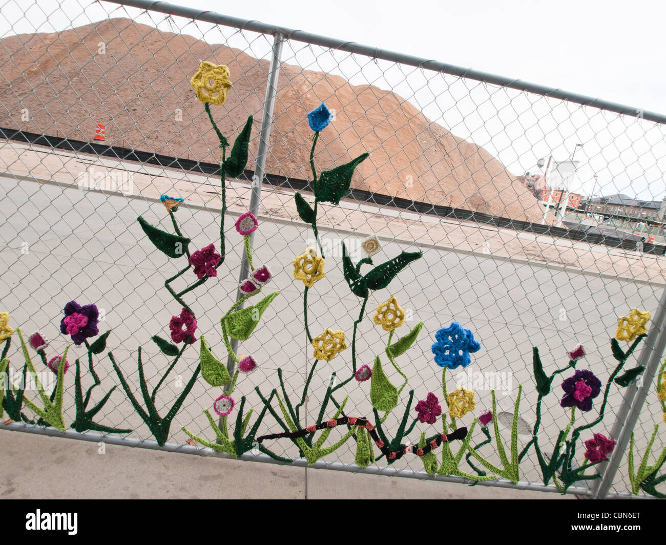 Construction fence covered with crocheted garden creatures like bugs ...