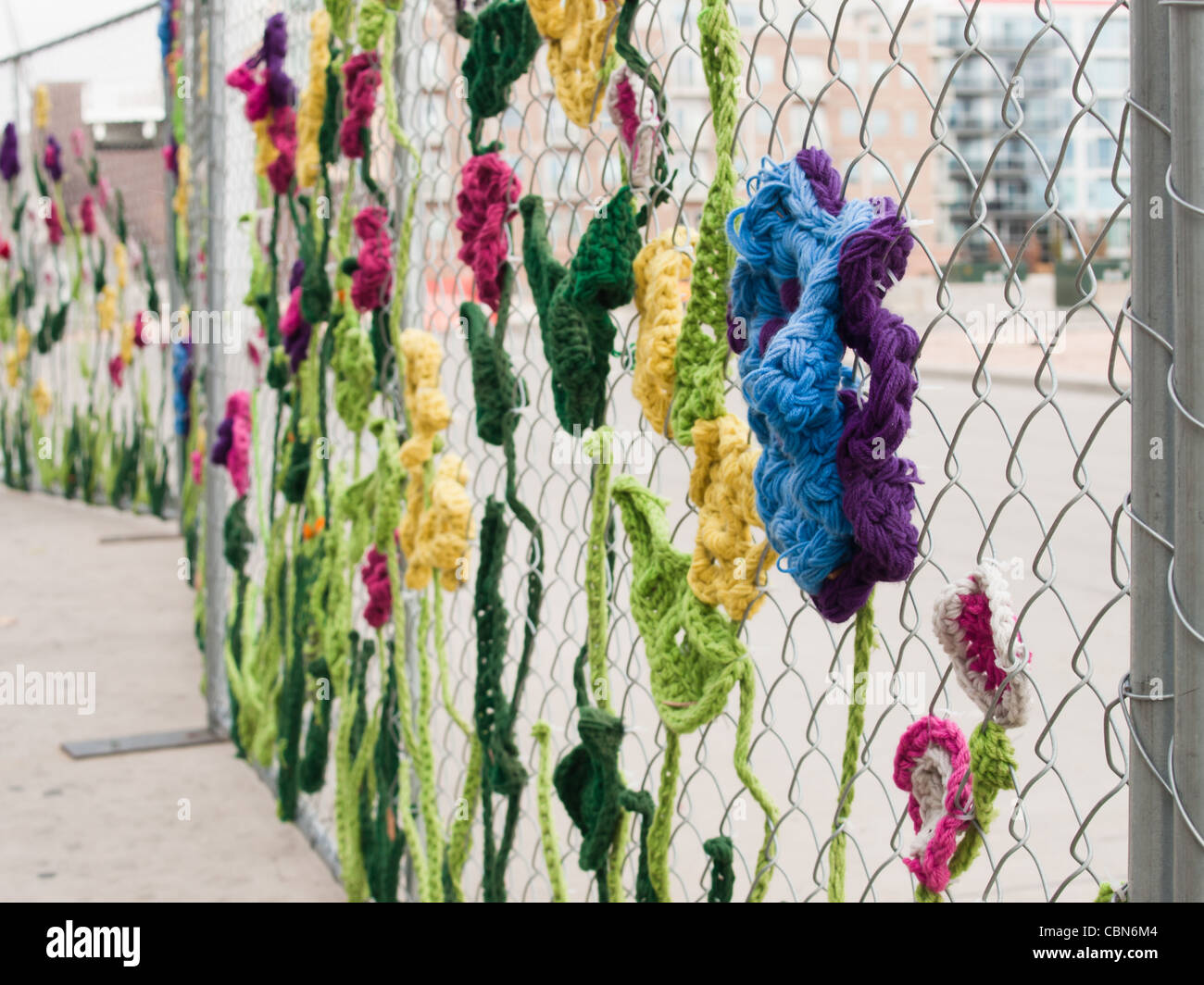 Construction fence covered with crocheted garden creatures like bugs ...