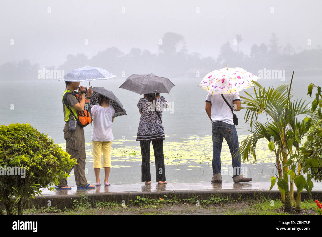 Tourists with umbrellas on a rainy day walk on a path at Beretan Lake ...