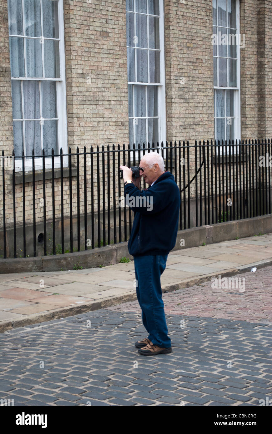 Old man holding camera taking photograph in old cobbled street in ...