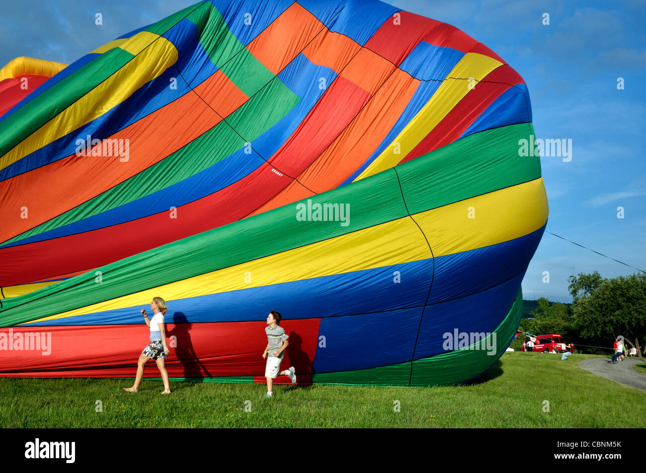 A hot air balloon being inflated on a grassy field with people walking ...