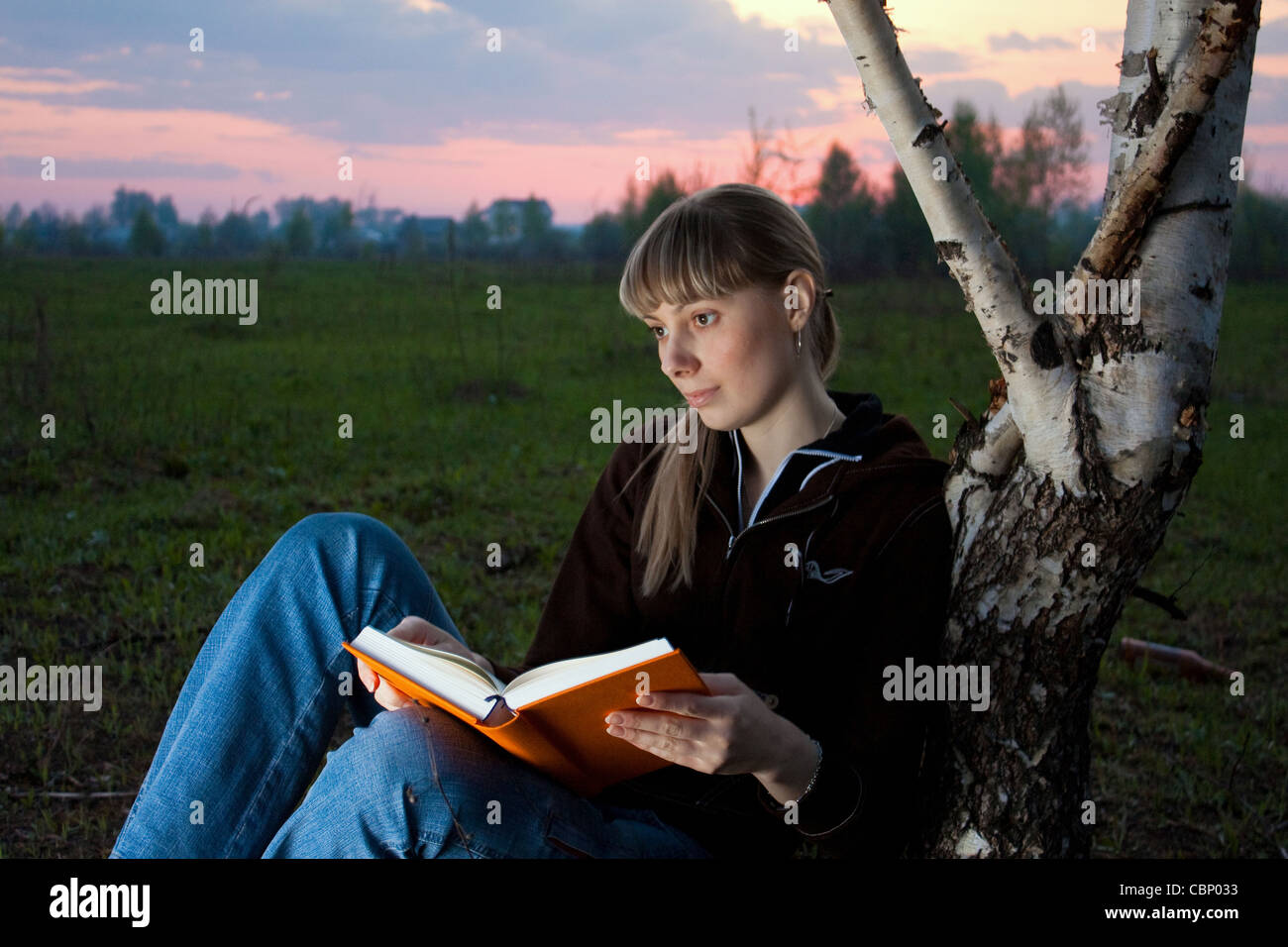 girl reading book and sitting outdoor under the tree with sky in ...
