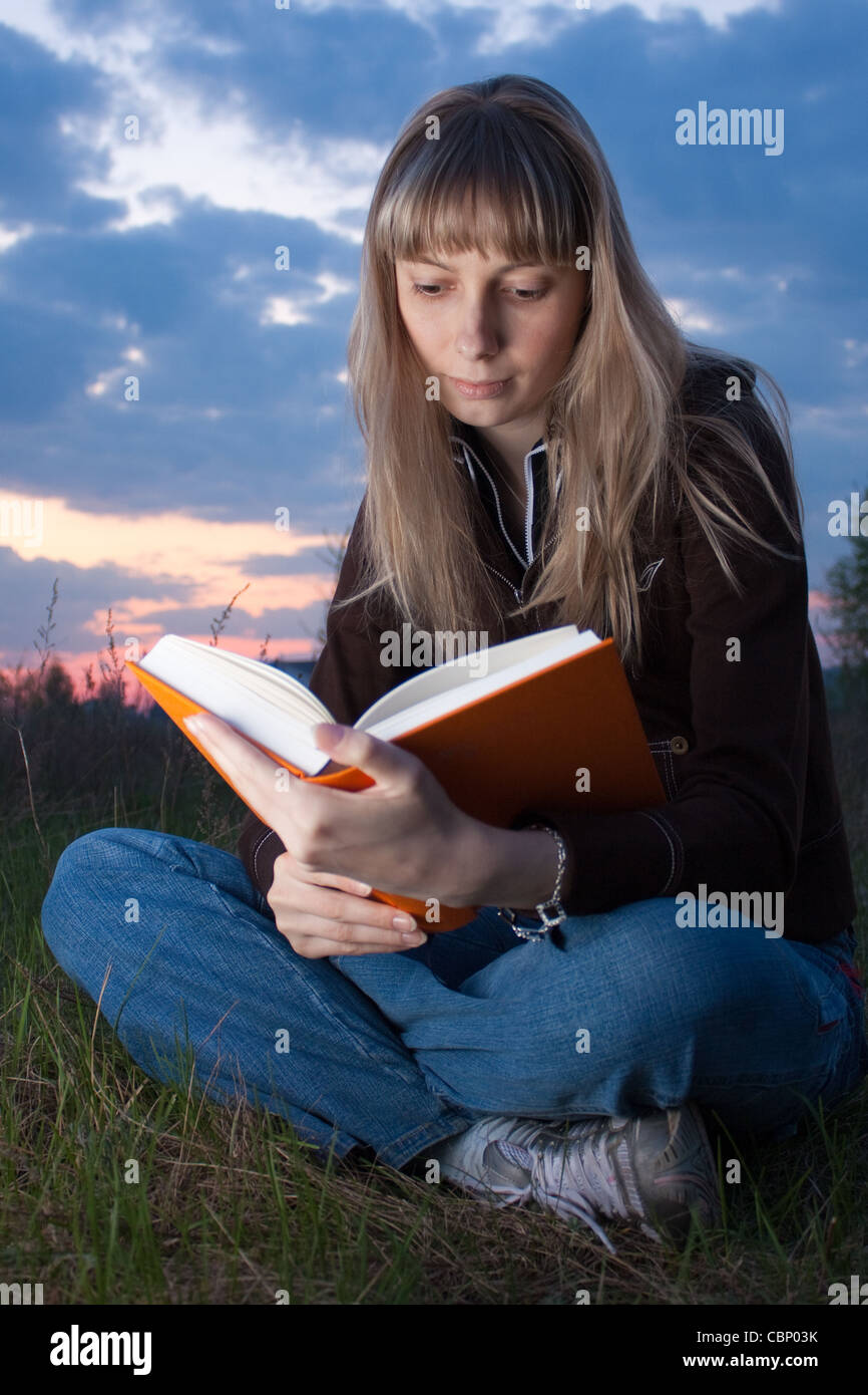 girl reading book and sitting outdoor under the tree with sky in ...