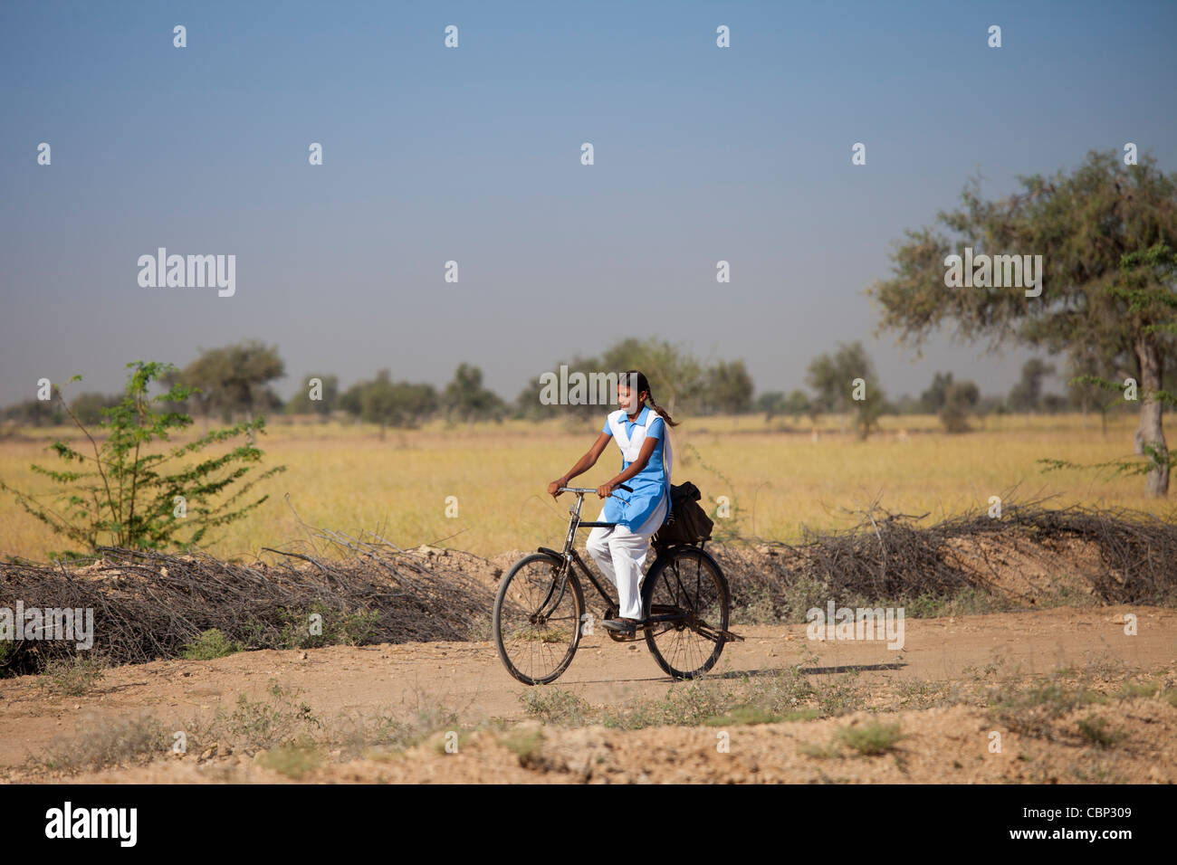 Young Indian girl in school uniform riding bicycle to her school near ...