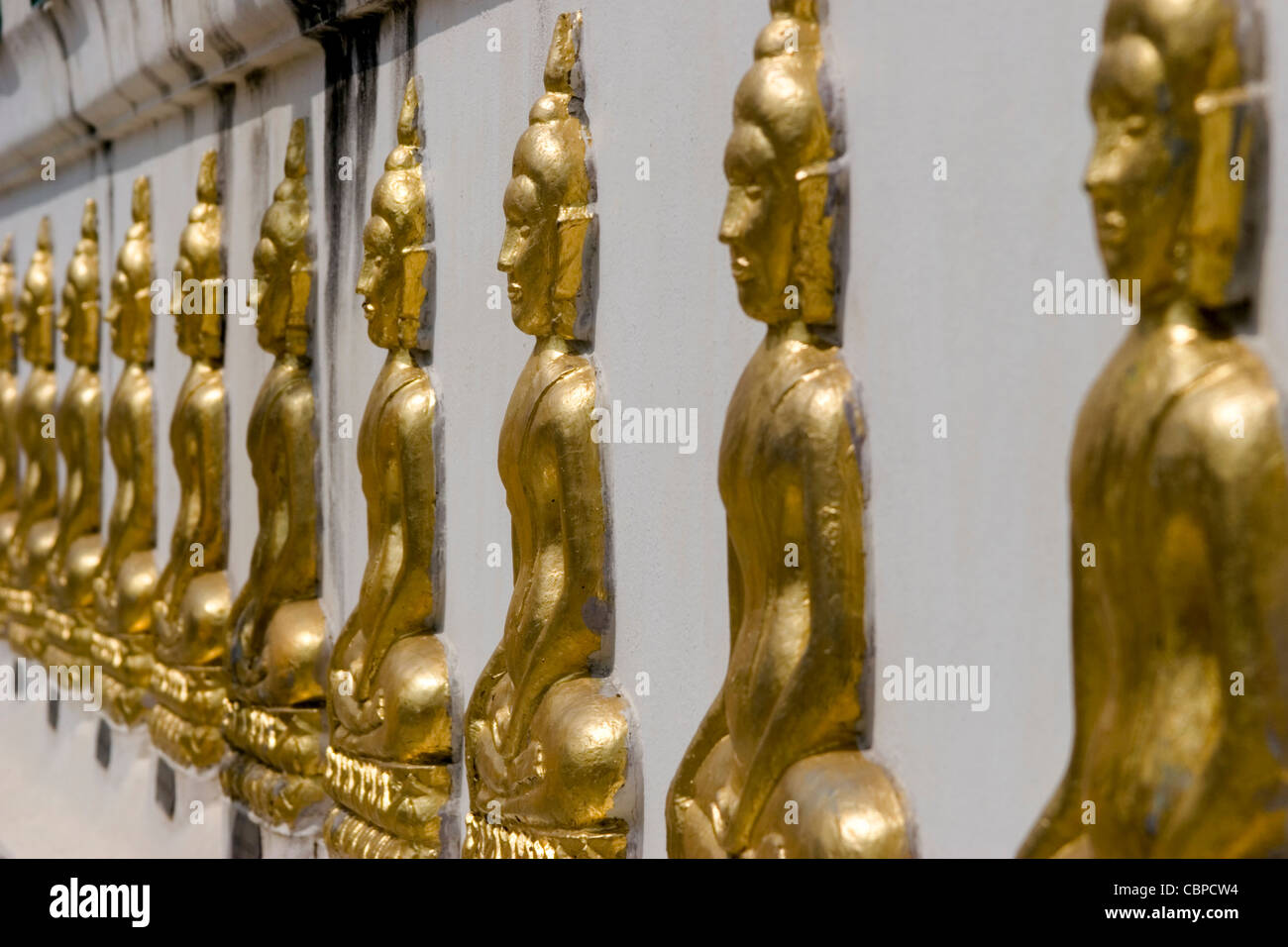 A row of gold Buddhist statues line a wall of an ancient and historic ...