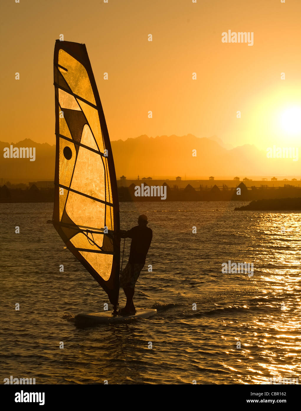silhouette of man on sailing windsurf on orange light of sunset ...