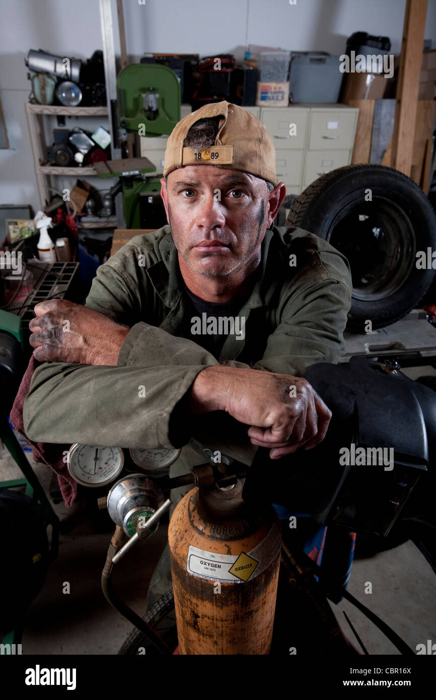 A grease covered blue collar working man takes a break, looking ...