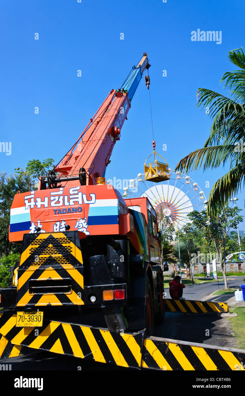 Tall multicolored crane rises in front of enormous Ferris wheel in blue ...