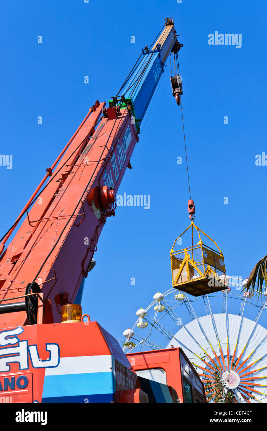Tall multicolored crane rises in front of enormous Ferris wheel in blue ...