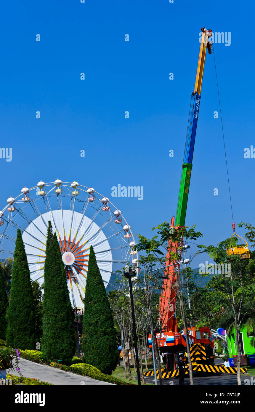 Tall multicolored crane rises in front of enormous Ferris wheel in blue ...