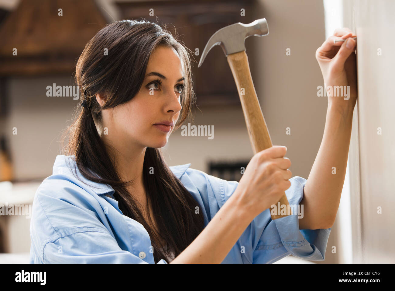 Caucasian woman hammering nail into wall Stock Photo - Alamy