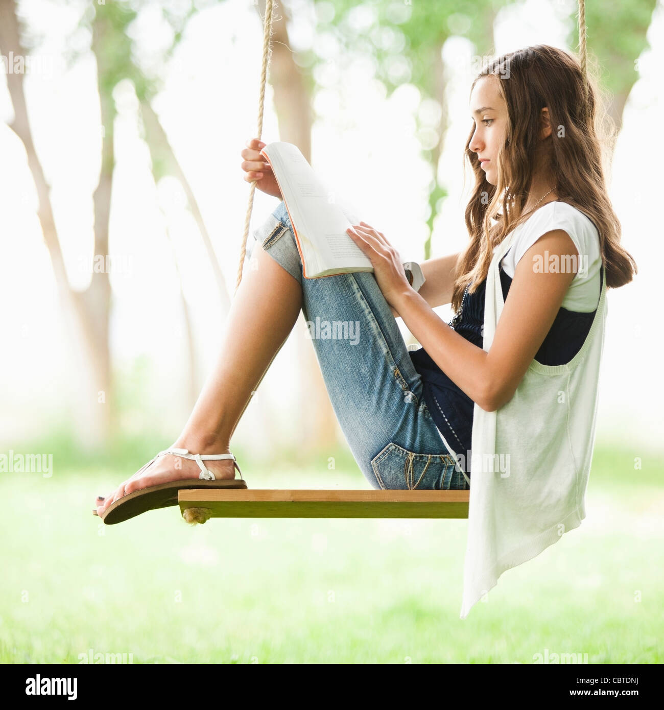 Caucasian girl reading book on swing Stock Photo - Alamy