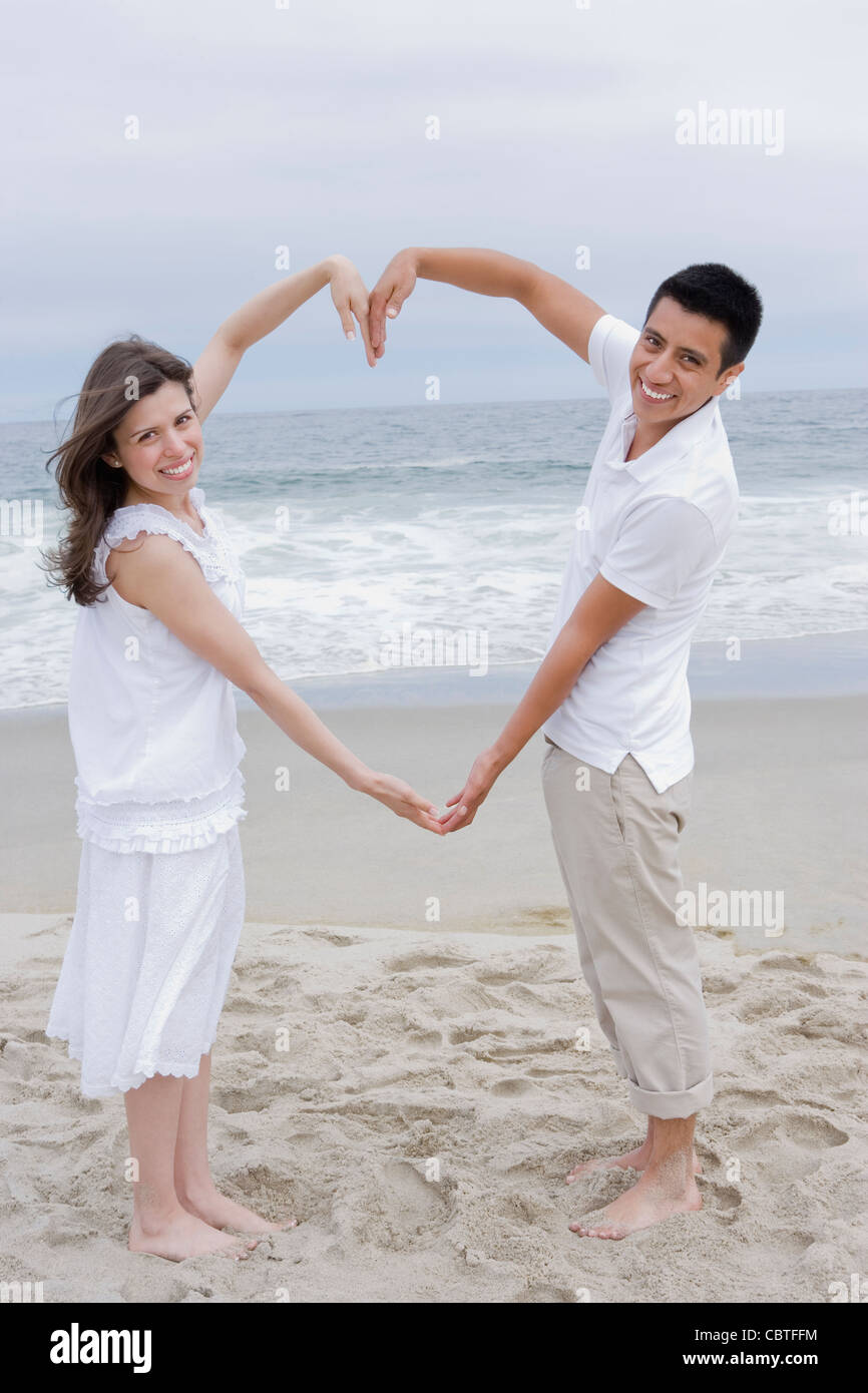 Hispanic couple making heart shape with arms on beach Stock Photo - Alamy