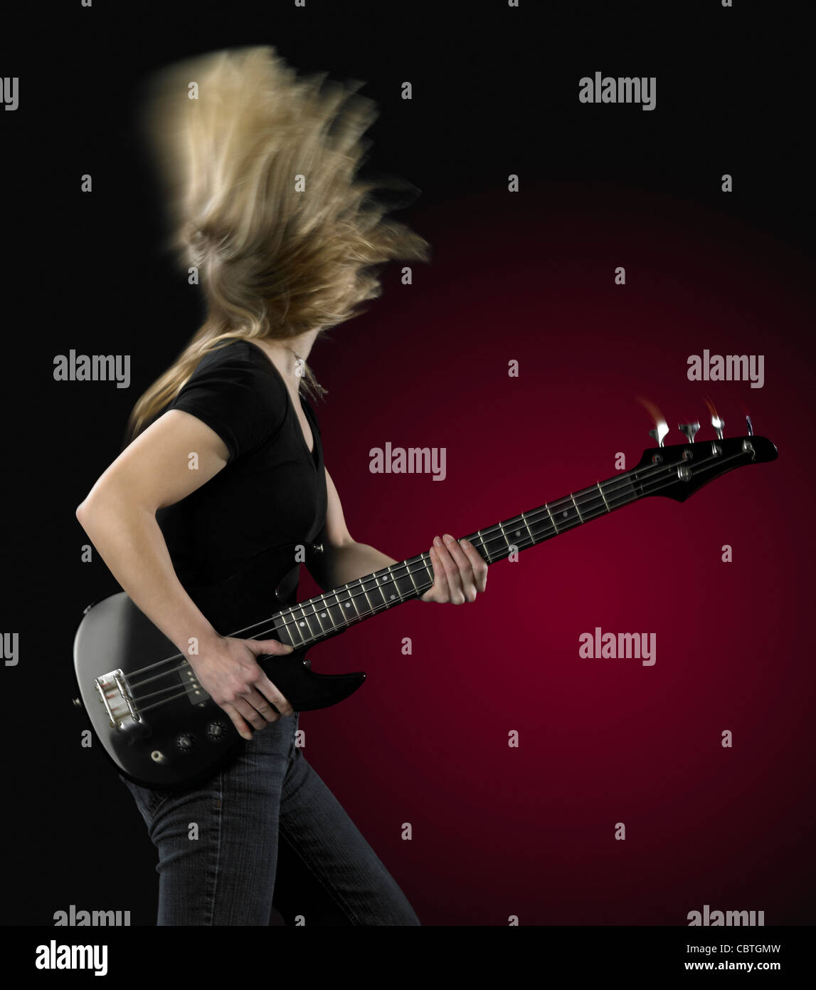 a woman playing a black bass guitar in front of partly reddish back ...