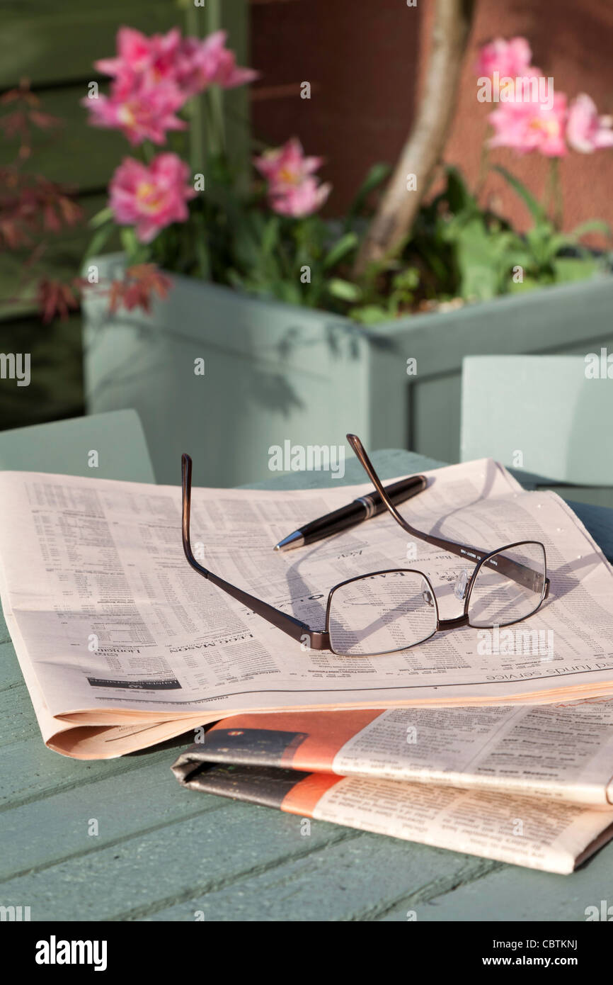 Still life of financial newspaper with spectacles and pen on garden ...