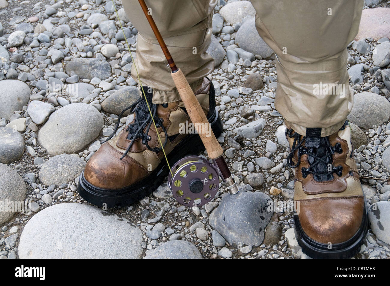 A fly fisherman readies his wading gear/boots and rod/reel for catching ...