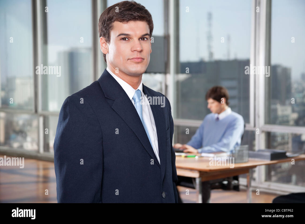 Portrait of confident male executive standing with colleague working in ...